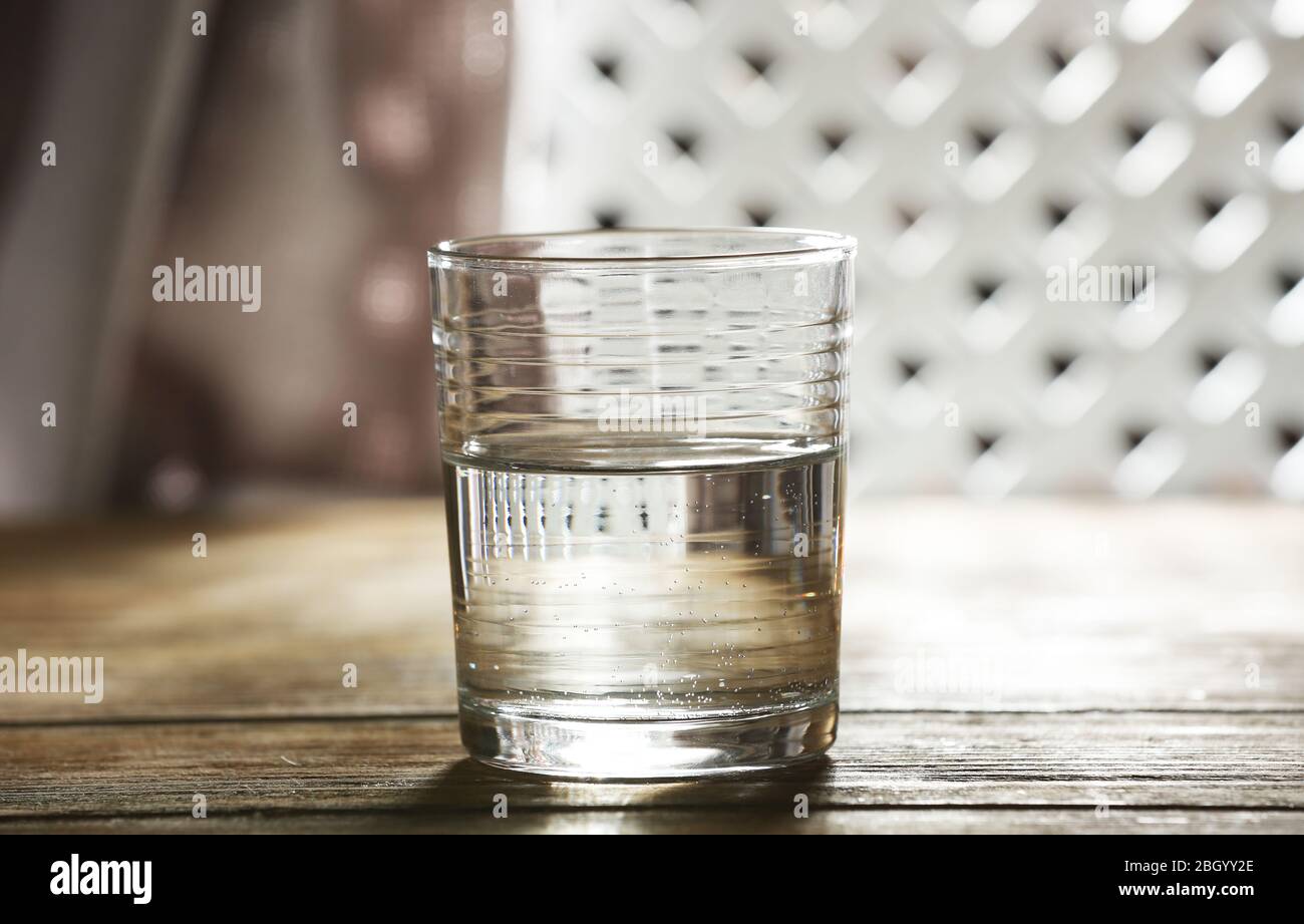 Glass of clean mineral water on wooden surface and lattice background ...