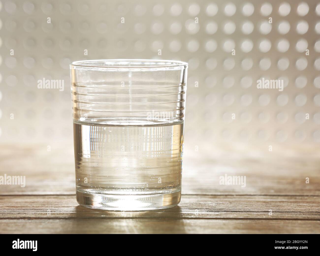 Glass of clean mineral water on wooden surface and lattice background ...
