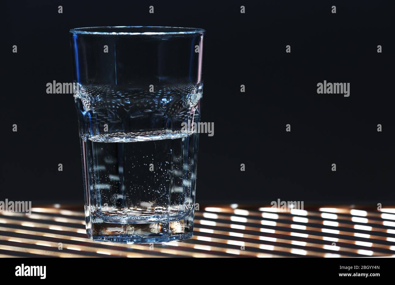 Glass of clean mineral water on lattice surface and dark color ...
