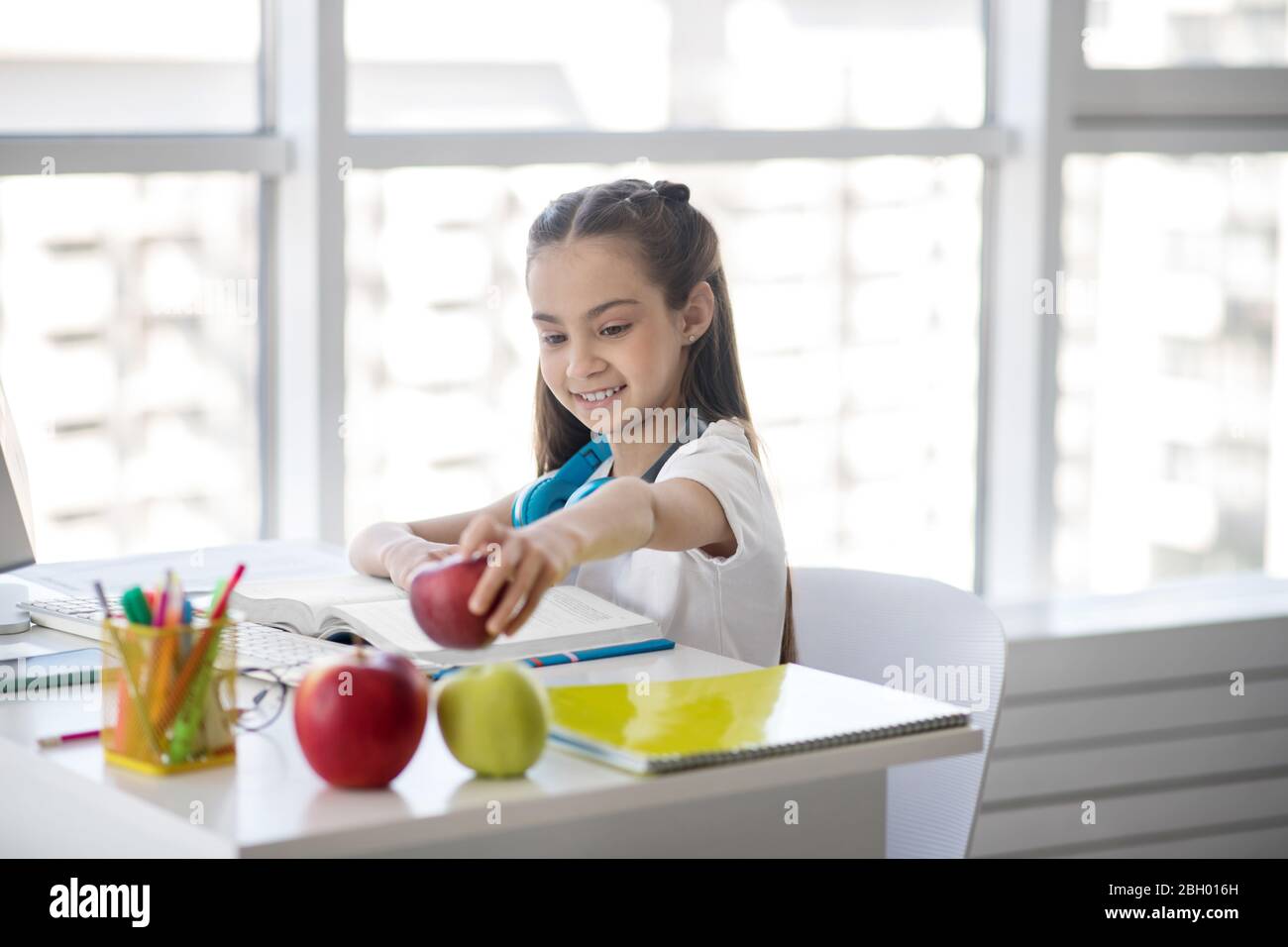 Cute dark-haired smiling girl taking an apple Stock Photo - Alamy