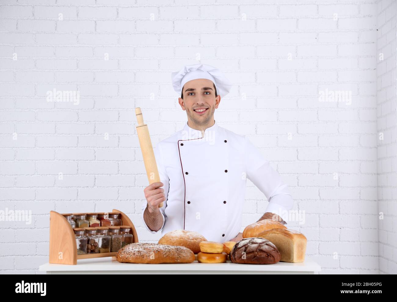 Baker in kitchen at table with freshly loaves of bread on white brick ...