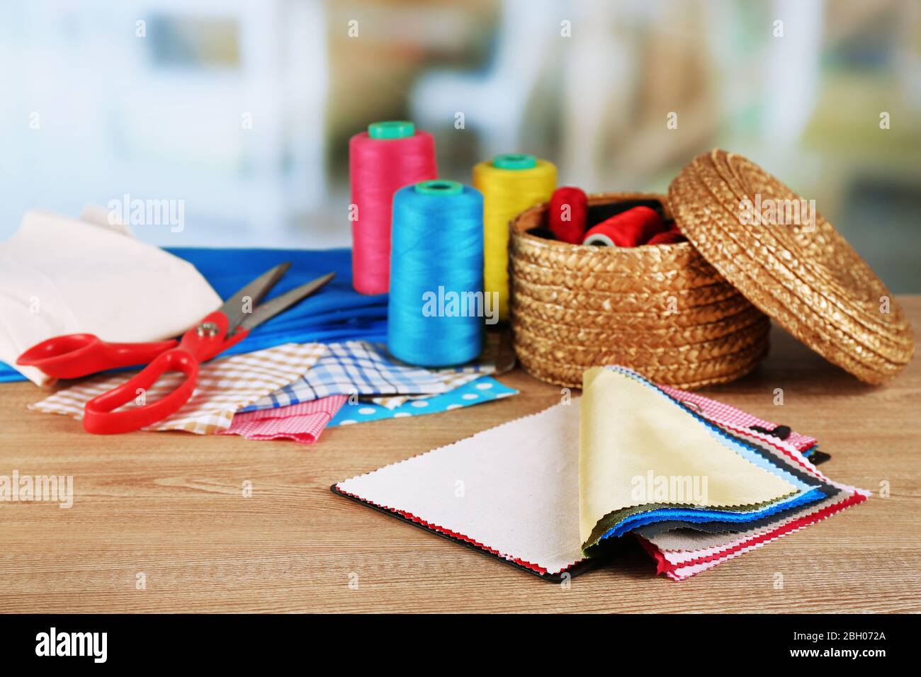 Colorful fabric samples and wicker basket of threads on wooden table ...