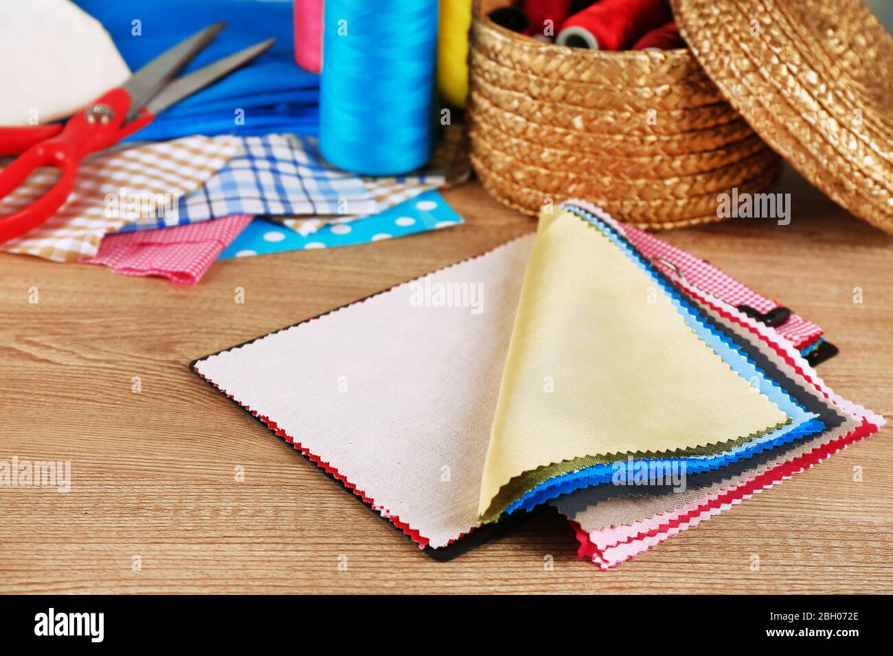 Colorful fabric samples and wicker basket of threads on wooden table ...