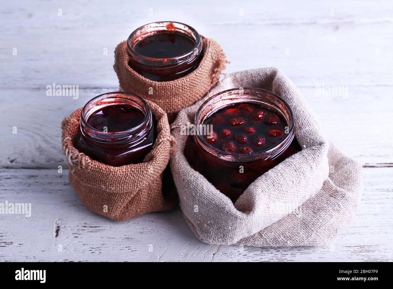 Homemade jars of fruits jam in burlap pouches on color wooden planks ...