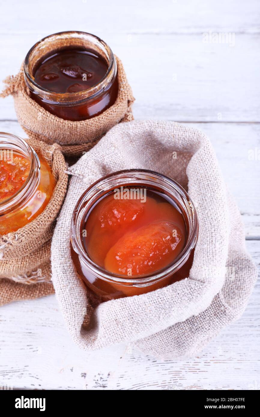 Homemade jars of fruits jam in burlap pouches on color wooden planks ...