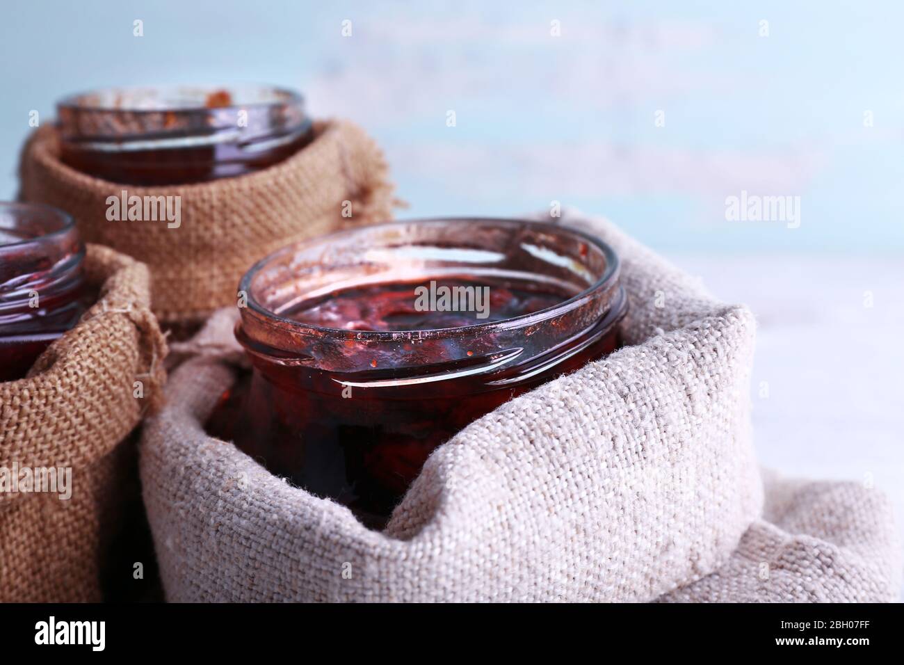 Homemade jars of fruits jam in burlap pouches on wooden table and color ...