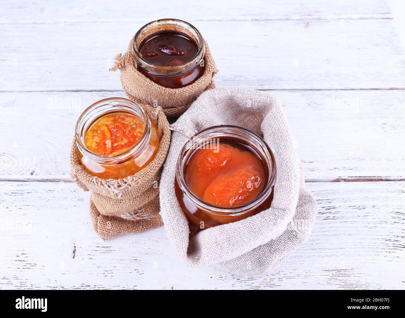Homemade jars of fruits jam in burlap pouches on color wooden planks ...