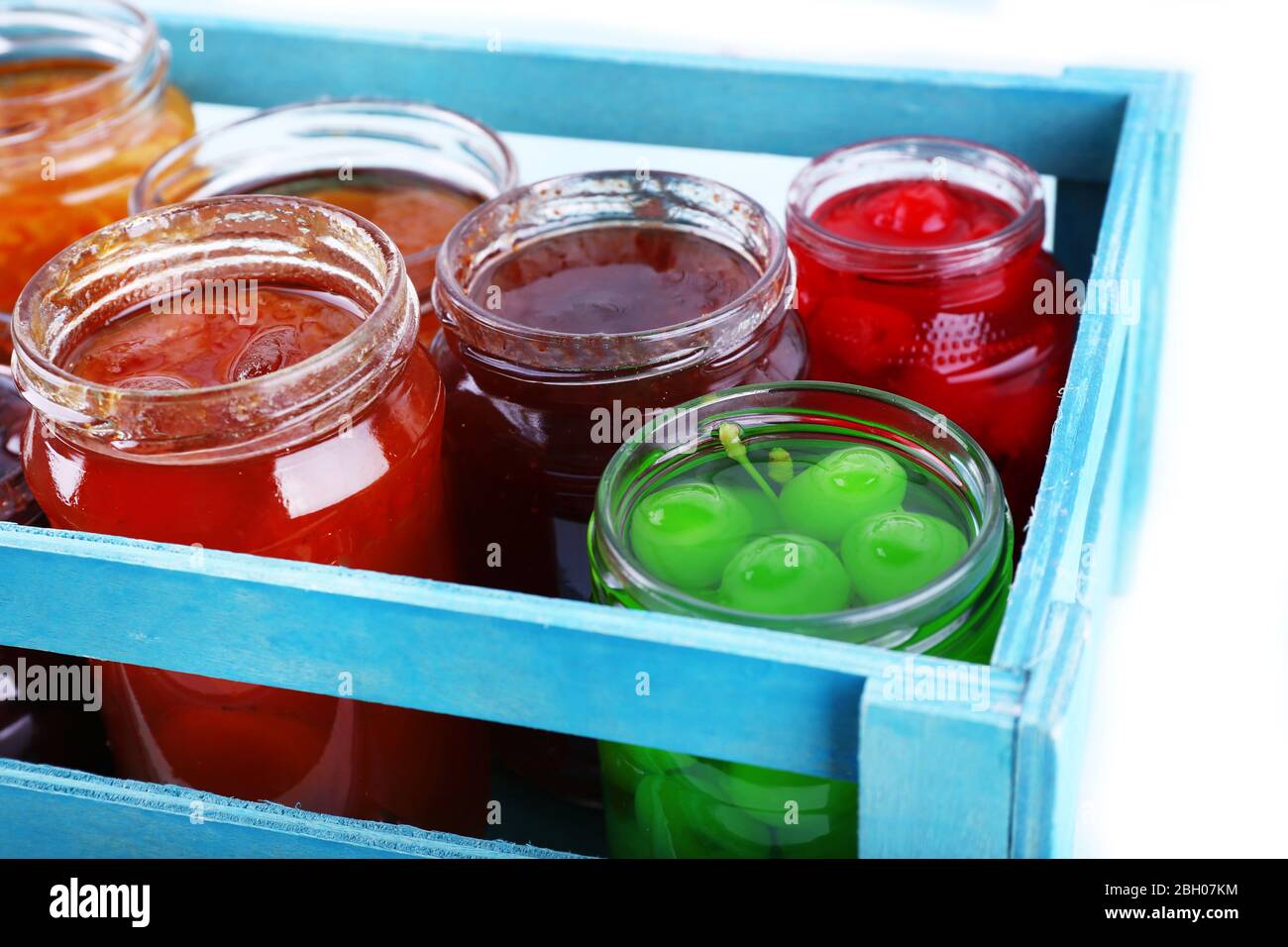 Homemade jars of fruits jam in crate on table and color wooden planks ...