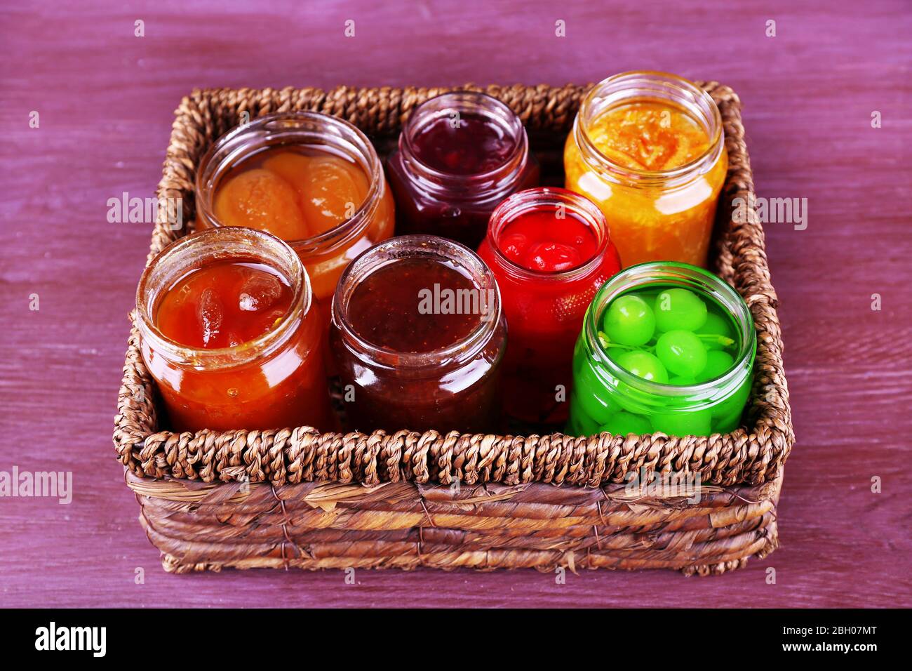 Homemade jars of fruits jam in wicker basket and color wooden ...