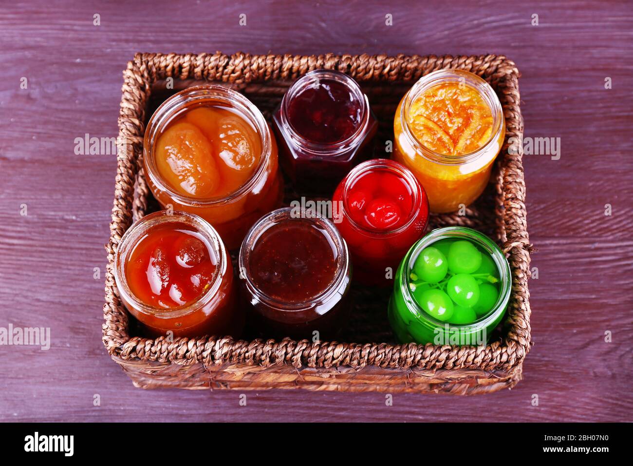 Homemade jars of fruits jam in wicker basket and color wooden ...