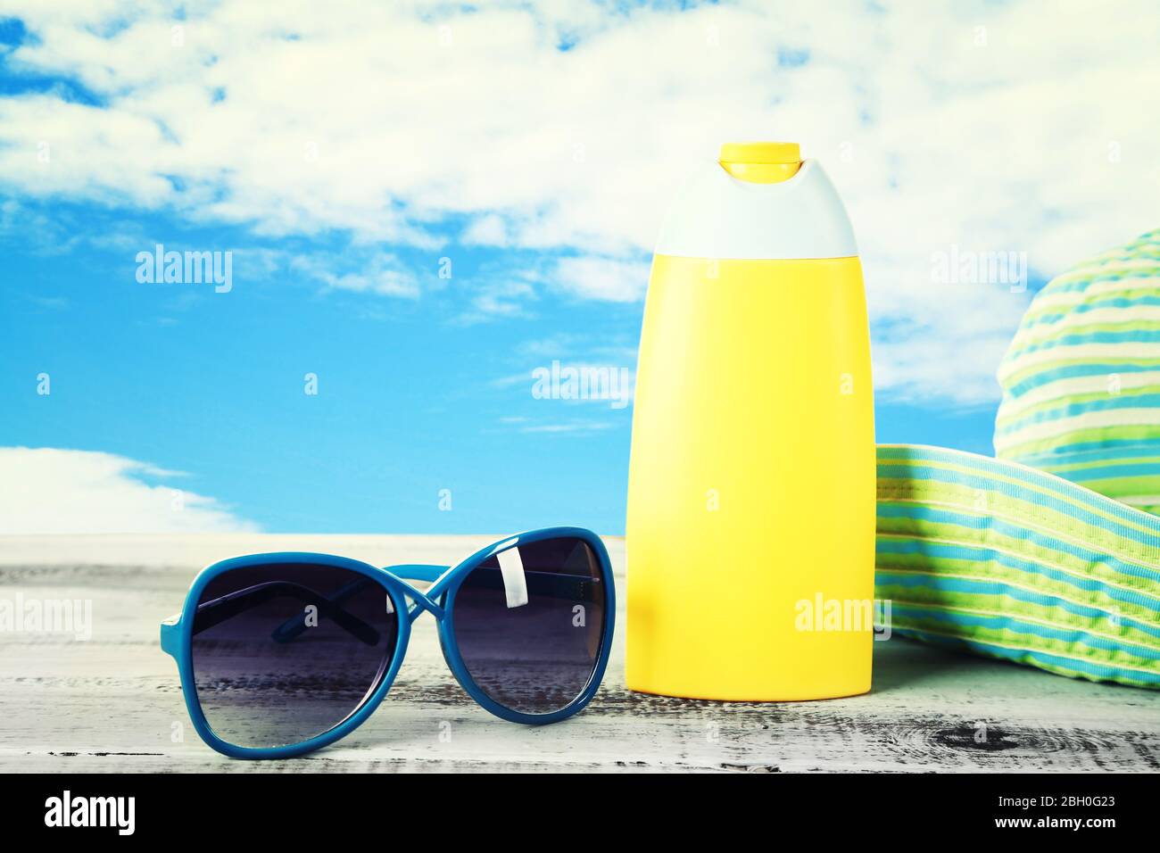 Bottle of suntan cream with sunglasses and hat on table isolated on ...