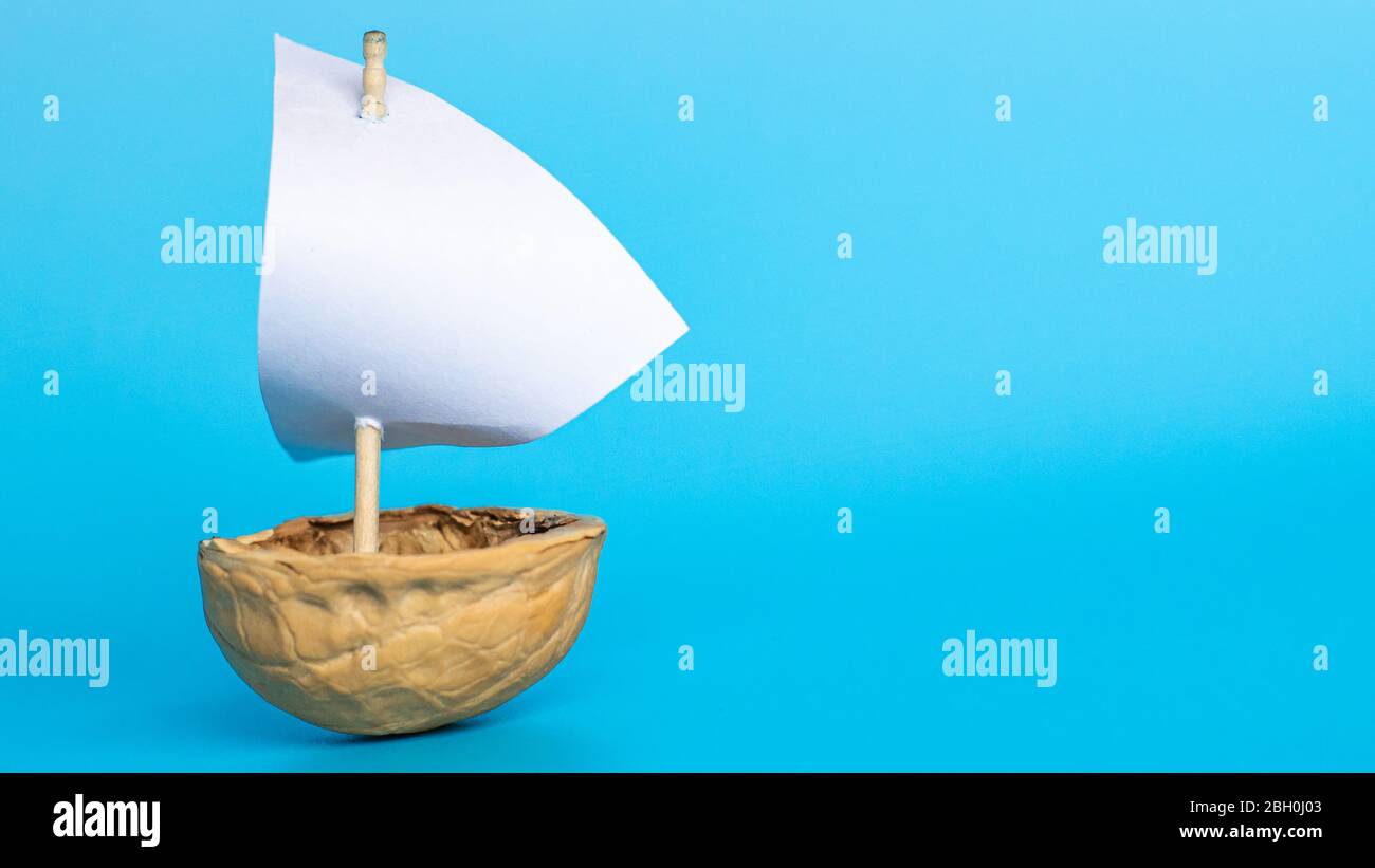 a boat made of nutshell with a white sail on the blue background ...