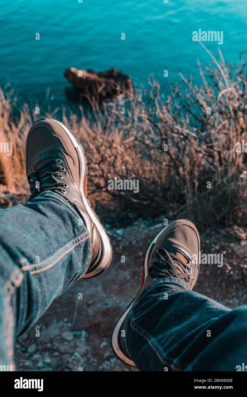 Legs of man in jeans and shoes are hanging from edge of cliff over the ...