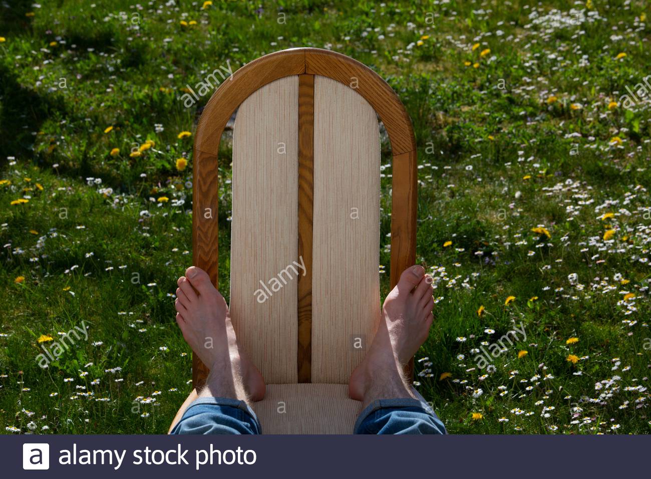 The feet of a young man relaxing on a chair in wram Spring sunshine in ...