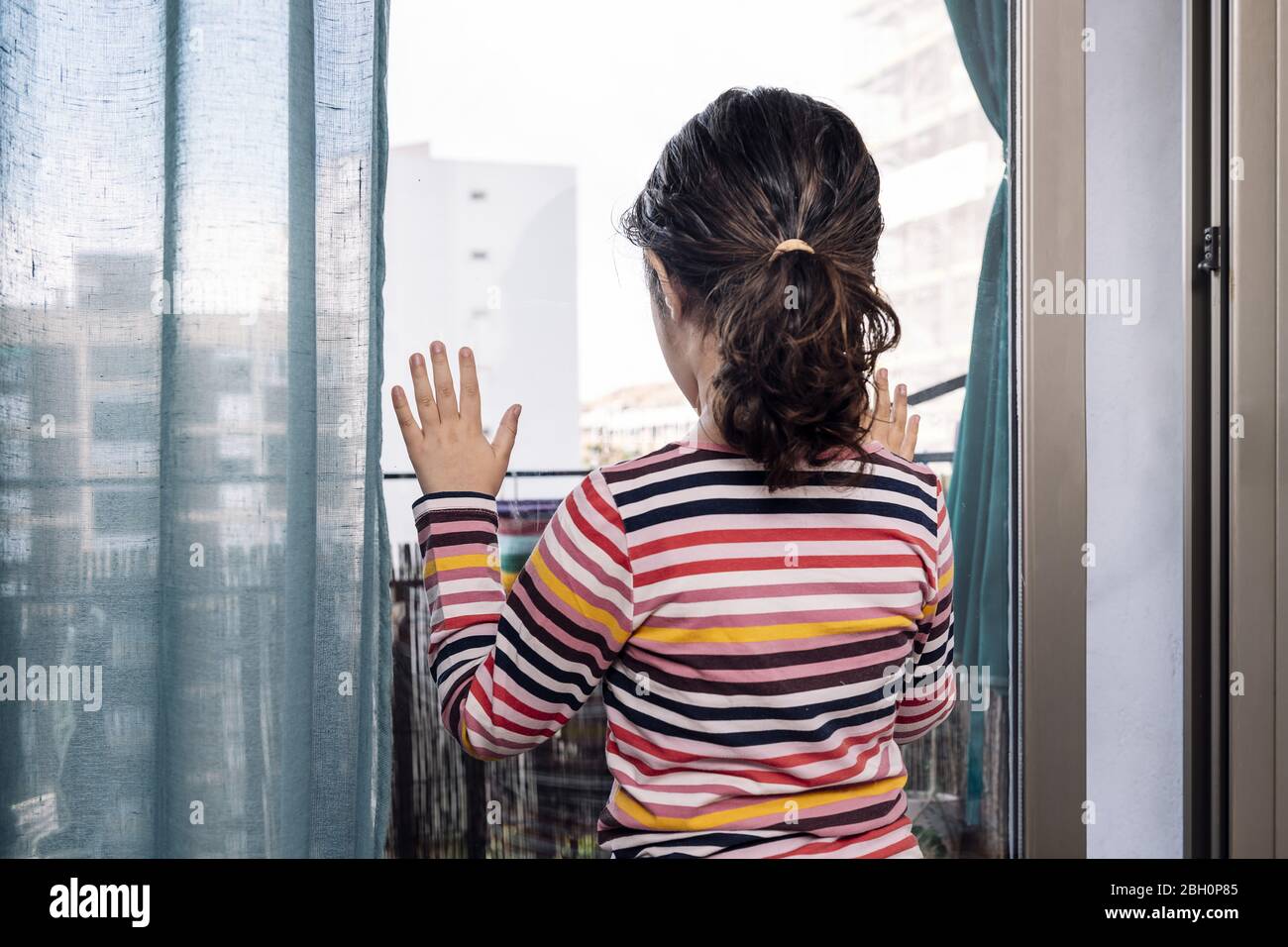 back view of an unrecognizable little girl looking through the window ...
