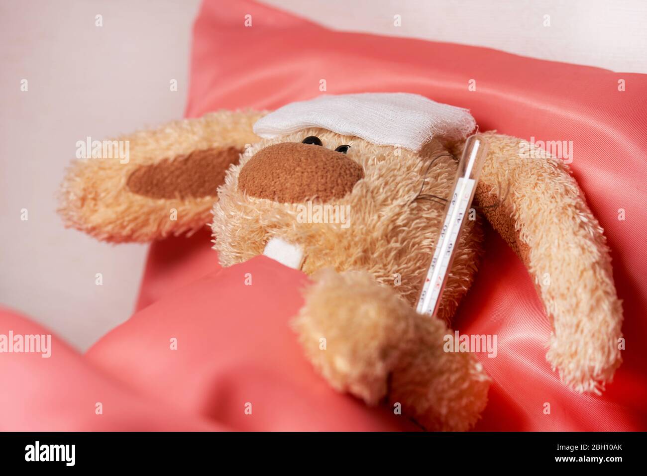 A sick stuffed rabbit with the flu measures the temperature in bed ...