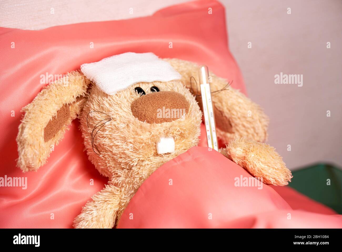 A sick stuffed rabbit with fever measures the temperature in bed Stock ...