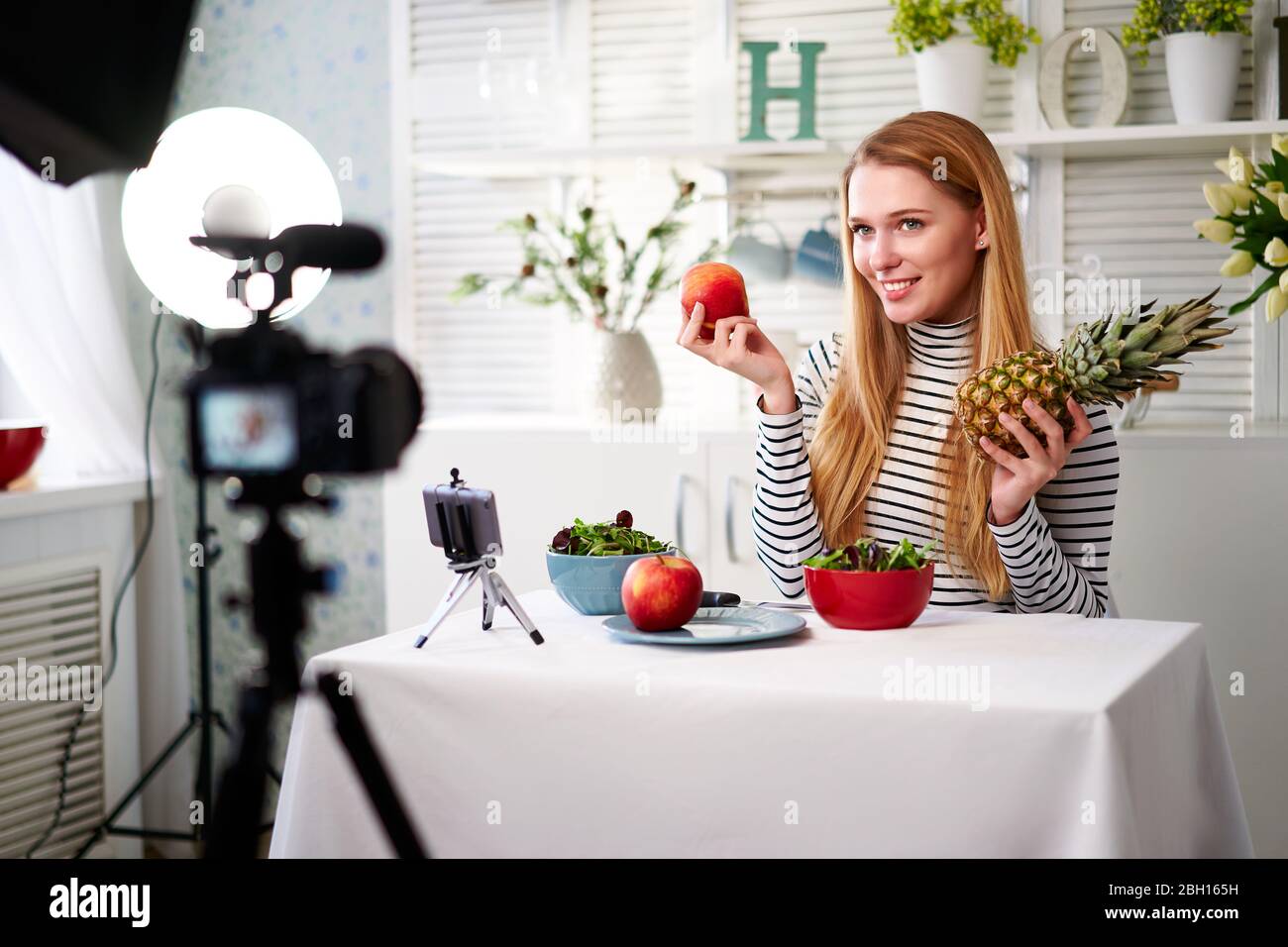 Food blogger cooking fresh vegan salad of fruits in kitchen studio ...