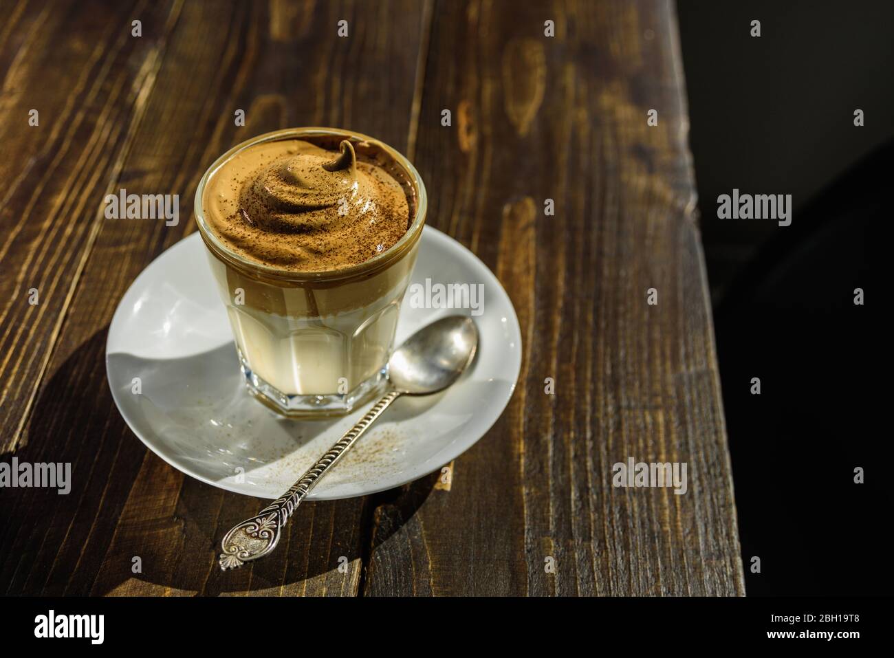 Dalgona instant coffee whipped drink in glass. Hard sun light, wooden ...