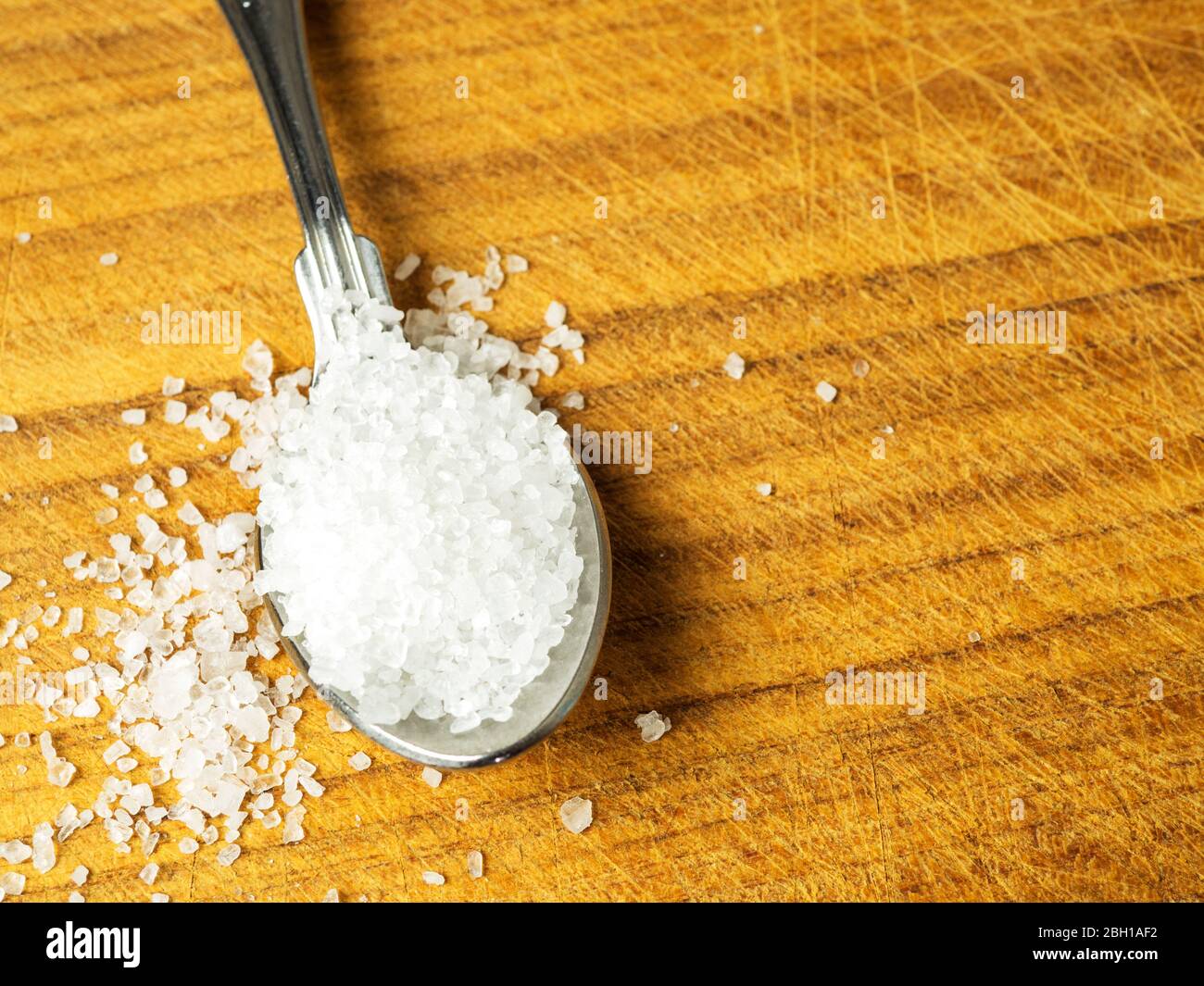 A teaspoonful of coarse sea salt on a wooden chopping board with a few ...