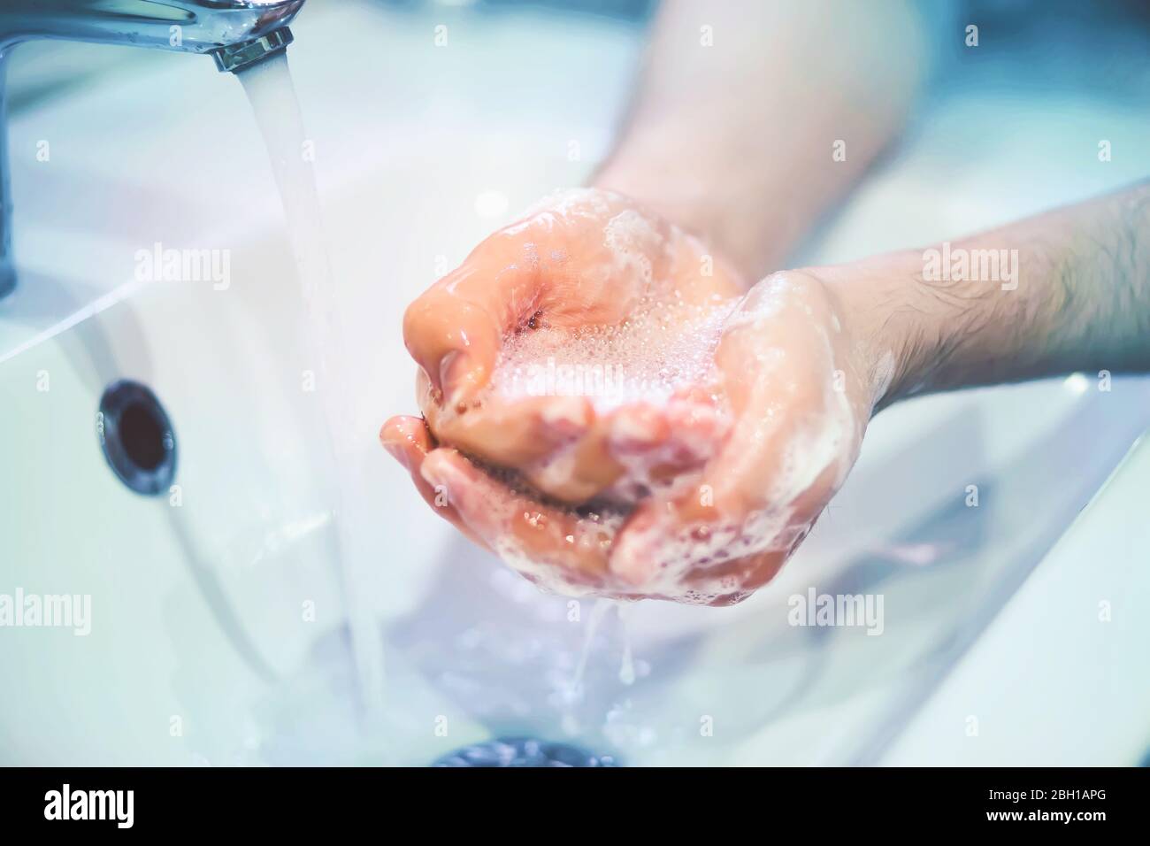 A man rinses his hands with soap suds under the flow of water from the ...