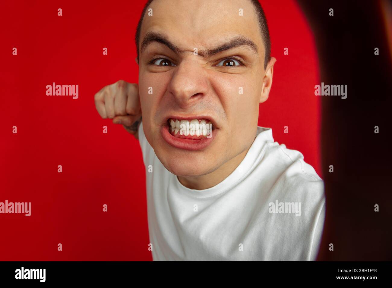 Angry kicking, close up. Caucasian young man's portrait isolated on red ...