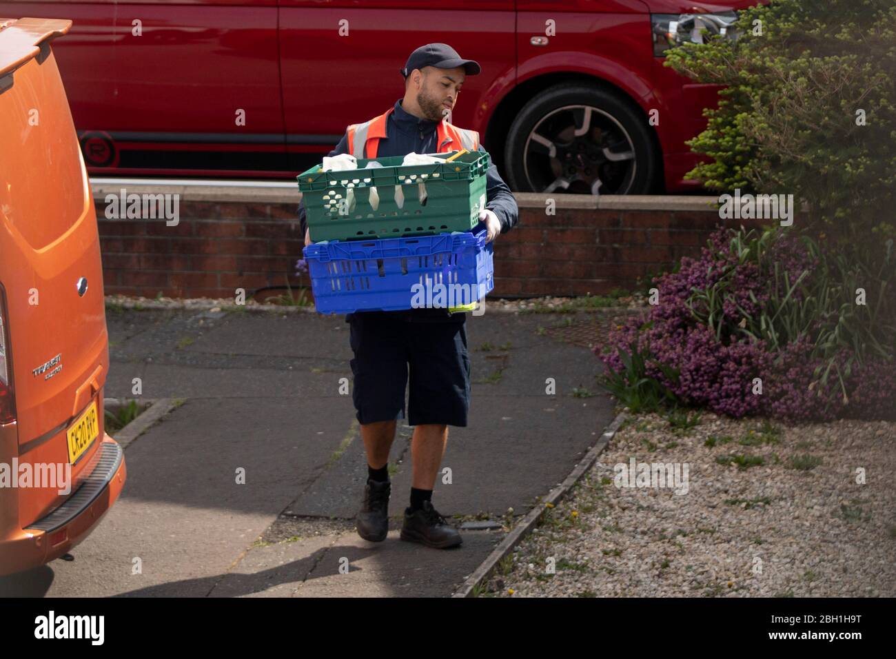 A Tesco home delivery worker carries crates of food to a front door in ...