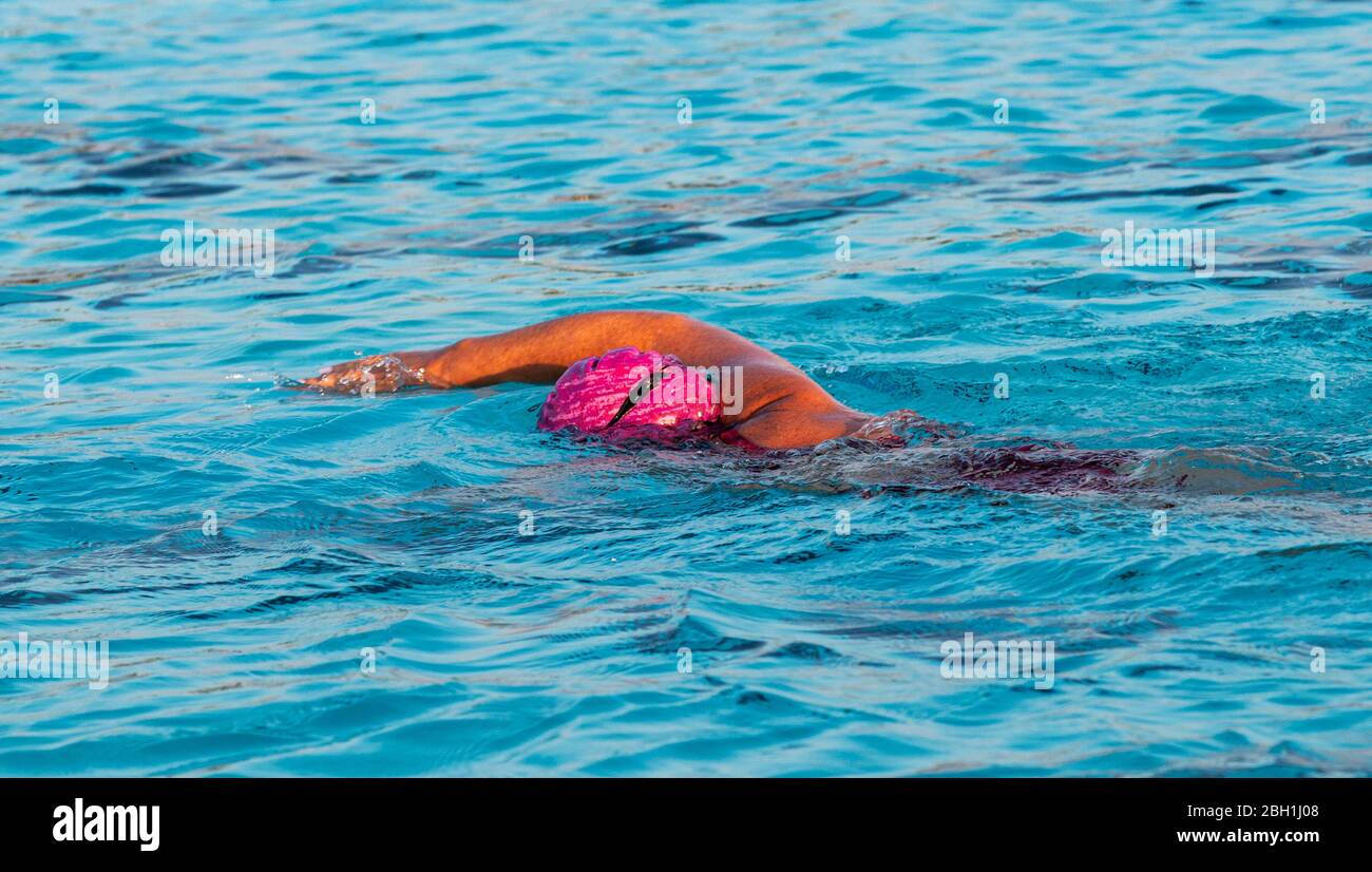A female swimmer in an outdoor pool freestyle swimming wearing a pink ...