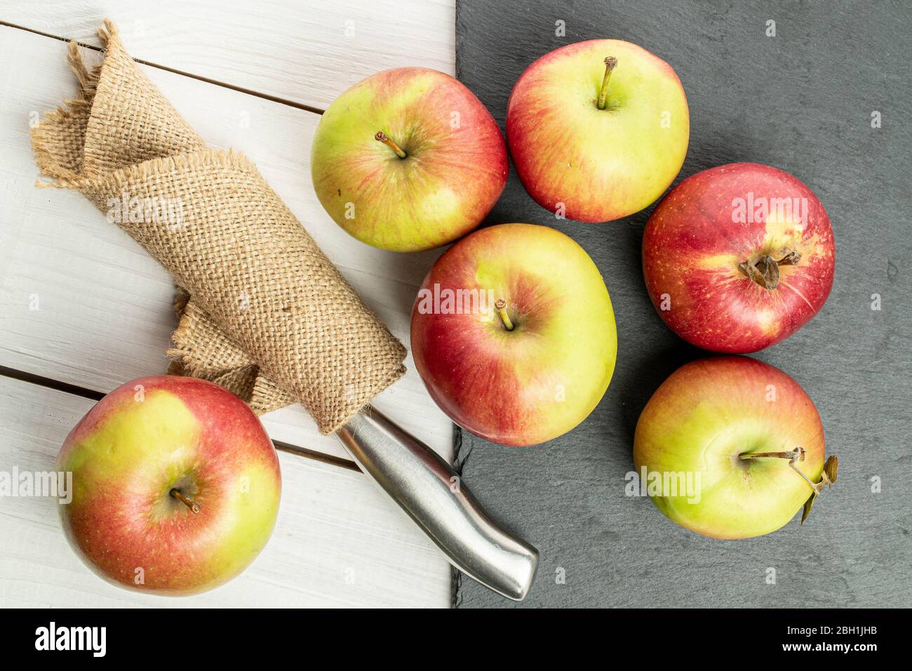 Group of six whole fresh garden apple on grey stone with knife in cloth ...