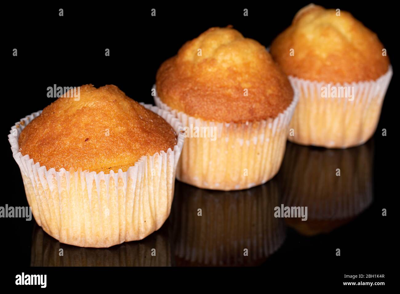 Group of three whole small baked muffin in row isolated on black glass ...