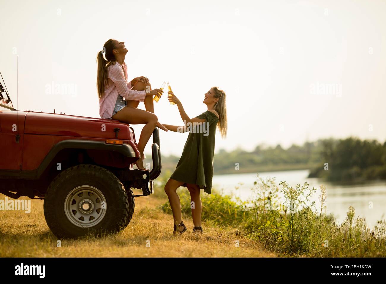 Two pretty happy young women drinking cider by the vehicle on the ...
