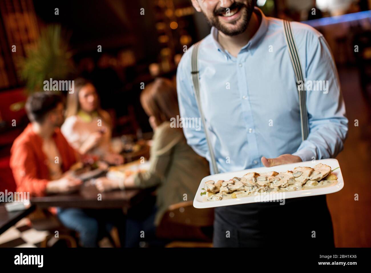 Smiling young waiter carrying plate with meat dish in the restaurant ...