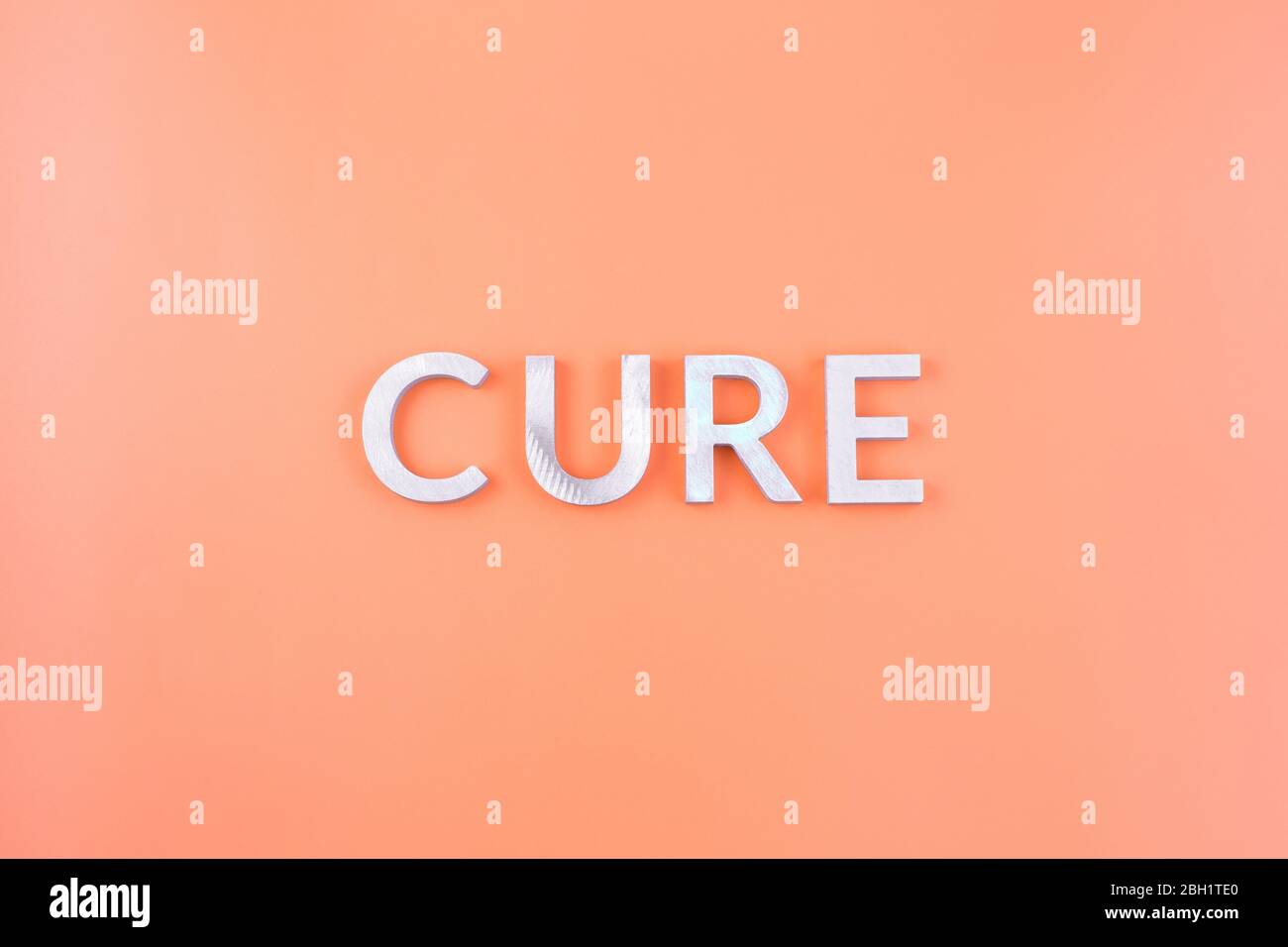 the word cure laid with thick aluminium letters on light orange pastel ...