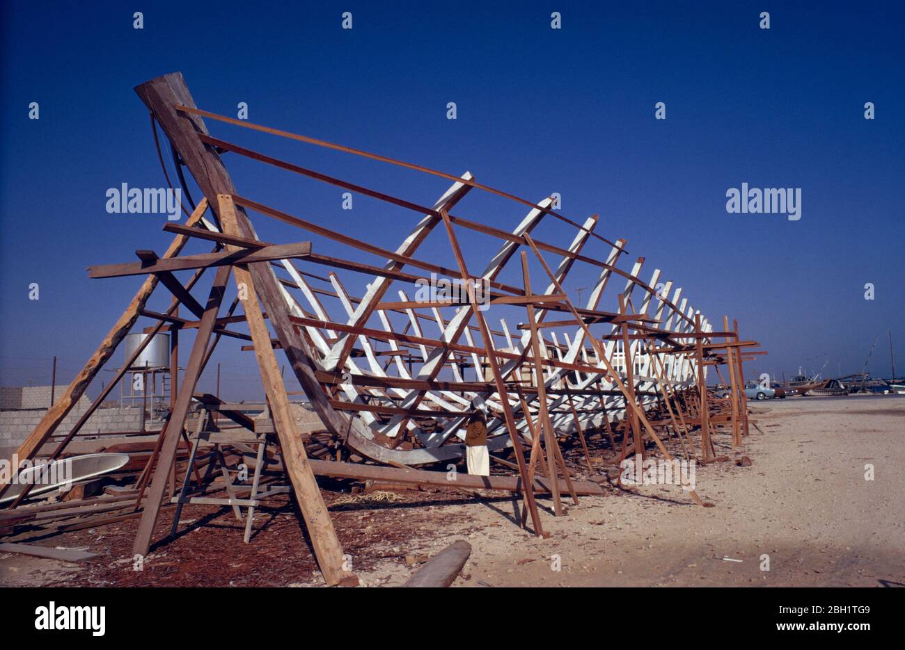 Qatar, Traditional dhow boat building, Man standing below wooden frame ...