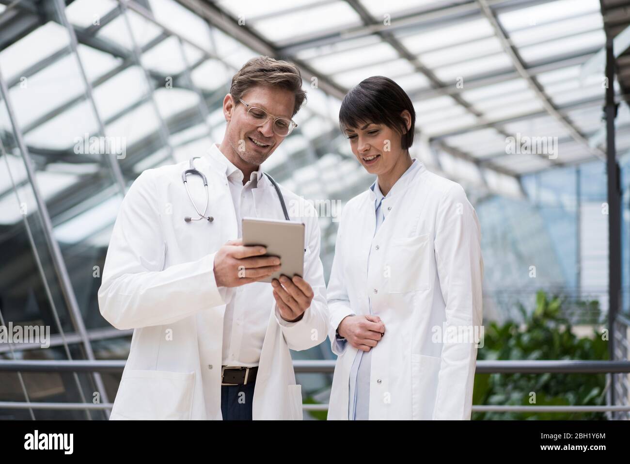 Doctor's standing in atrium, using digital tablet, discussing solutions ...