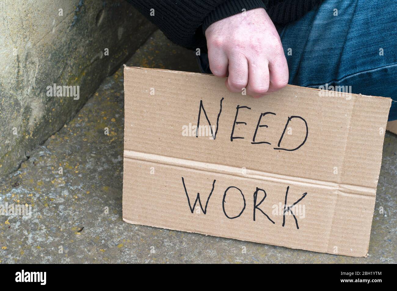 unemployed man sitting on the ground holding a cardboard sign saying ...