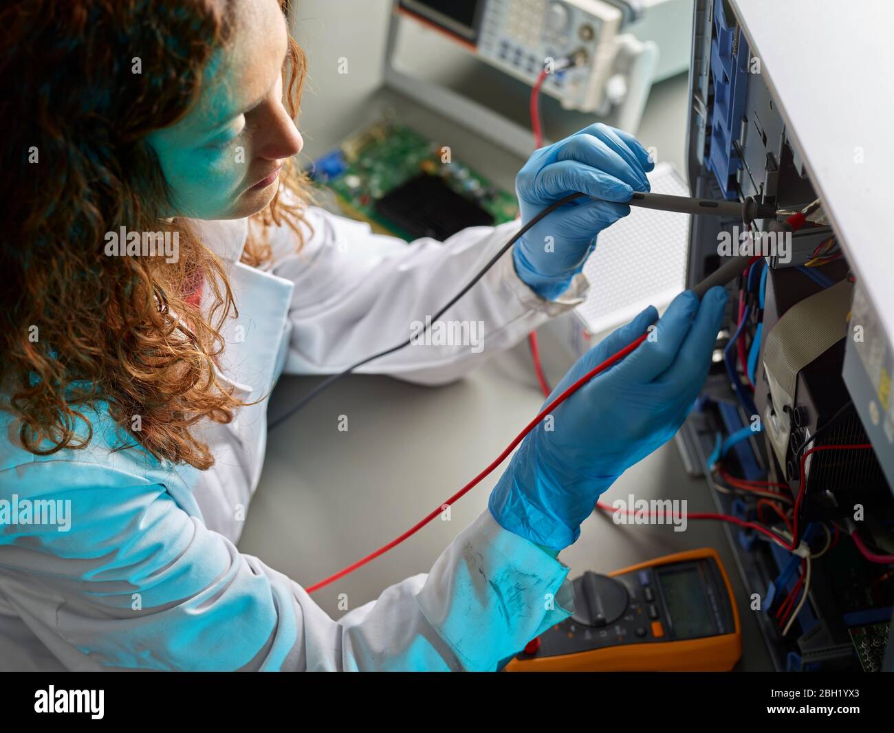 Female technichian working on open computer, using measuring device ...