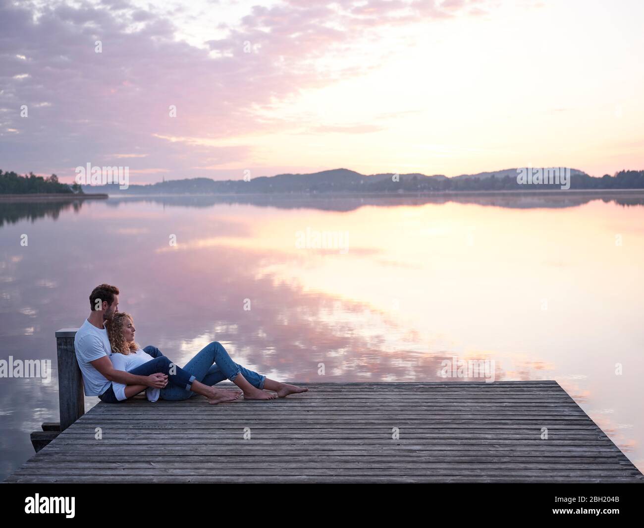 Romantic couple sitting on jetty at the lake Stock Photo - Alamy