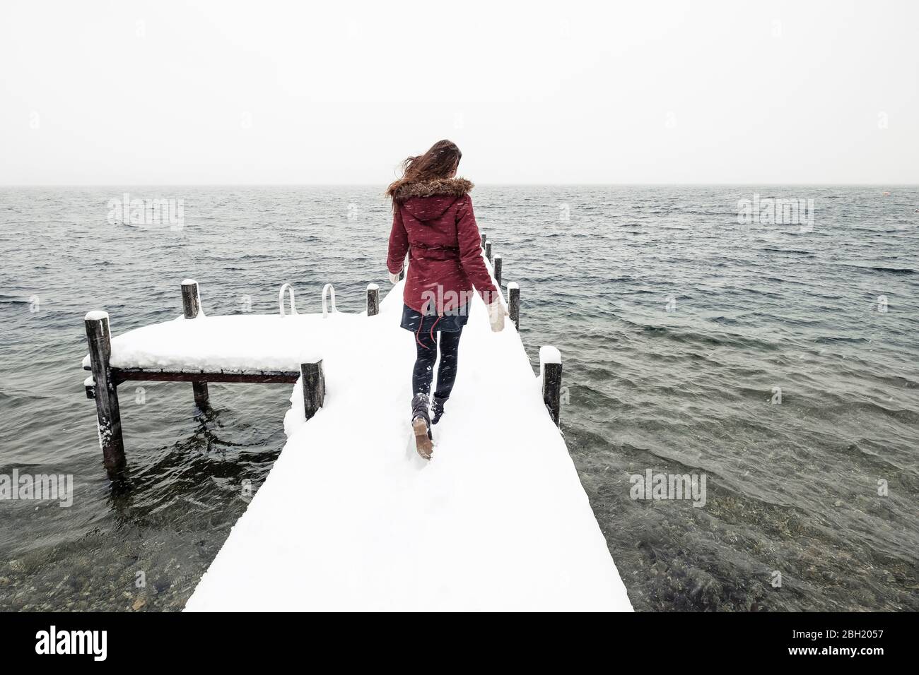 Back view of young woman running on snow-covered jetty at Lake ...
