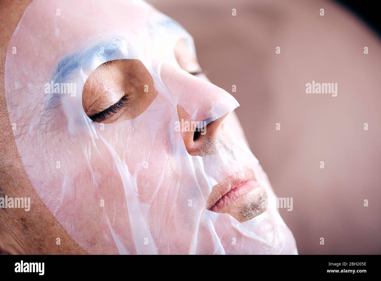 closeup of a handsome caucasian man wearing a bio-cellulose sheet mask ...