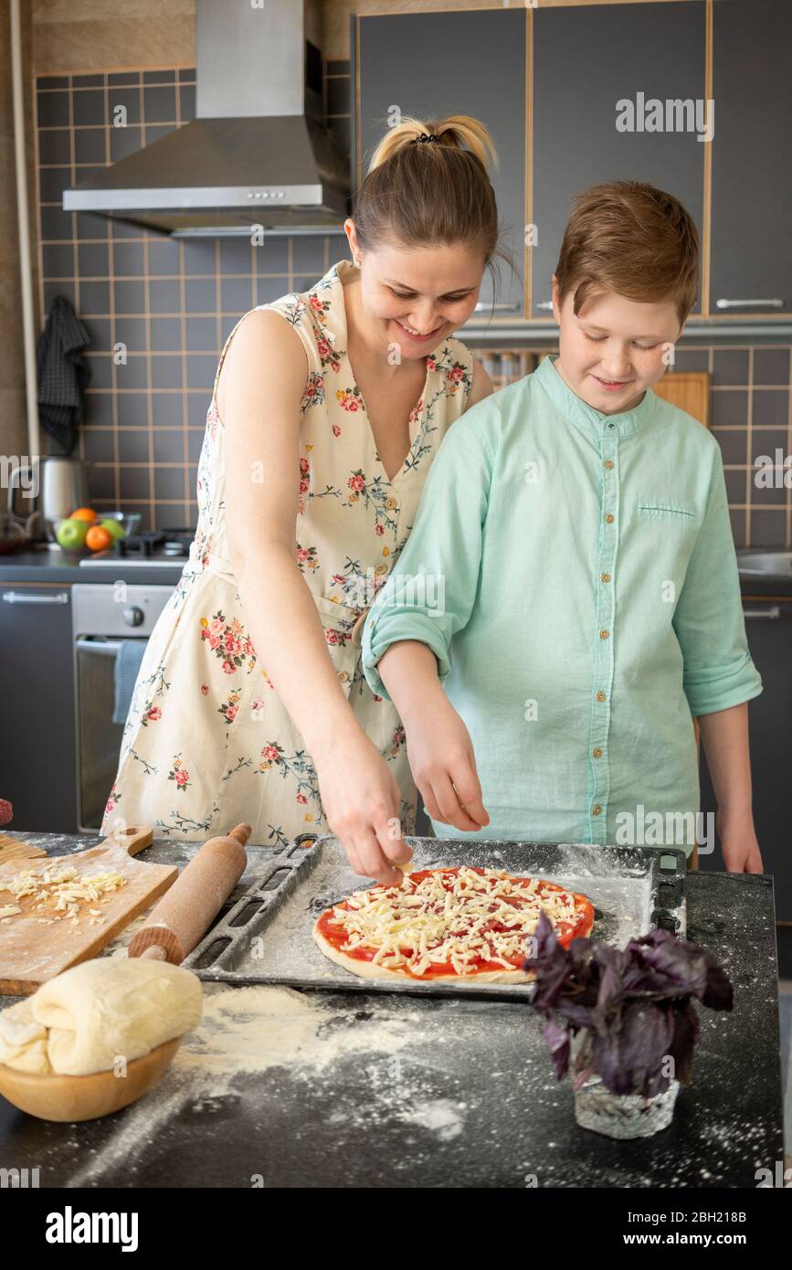 Mother and son scattering grated cheese on pizzy base Stock Photo - Alamy
