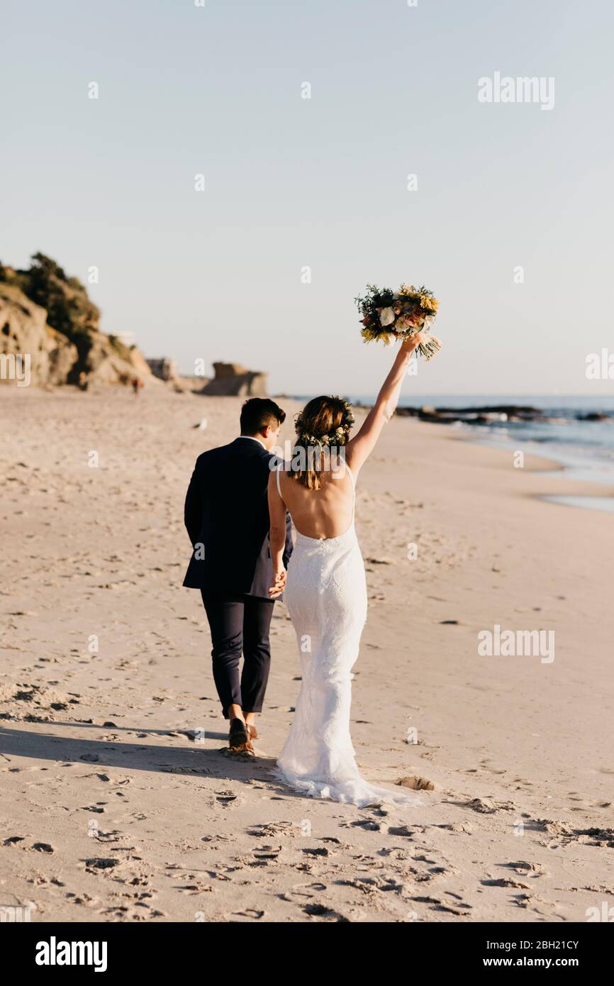 Rear view of happy bridal couple walking at the beach Stock Photo - Alamy