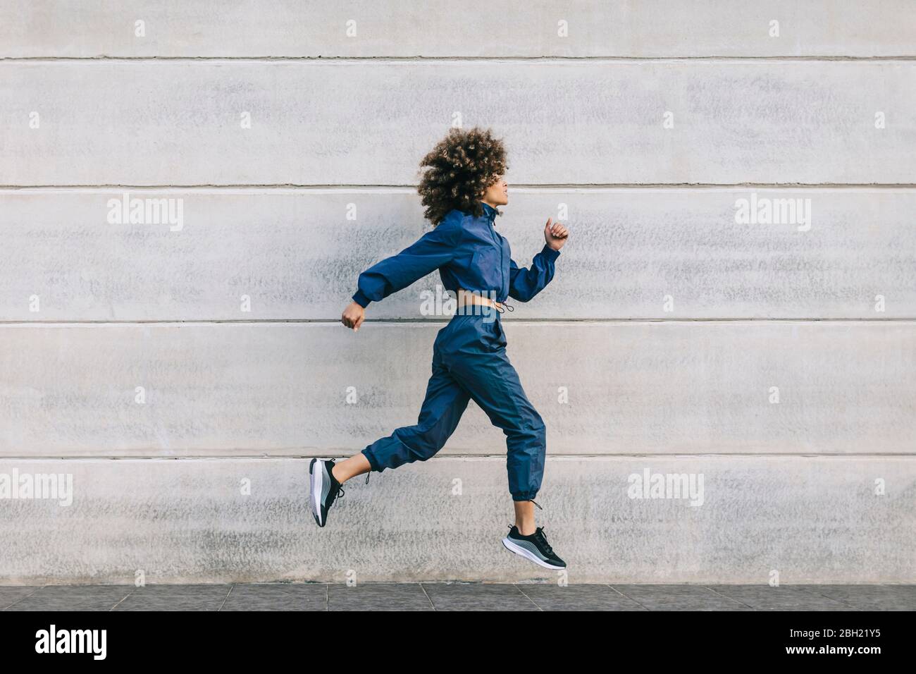 Stylish young woman running along concrete wall Stock Photo - Alamy