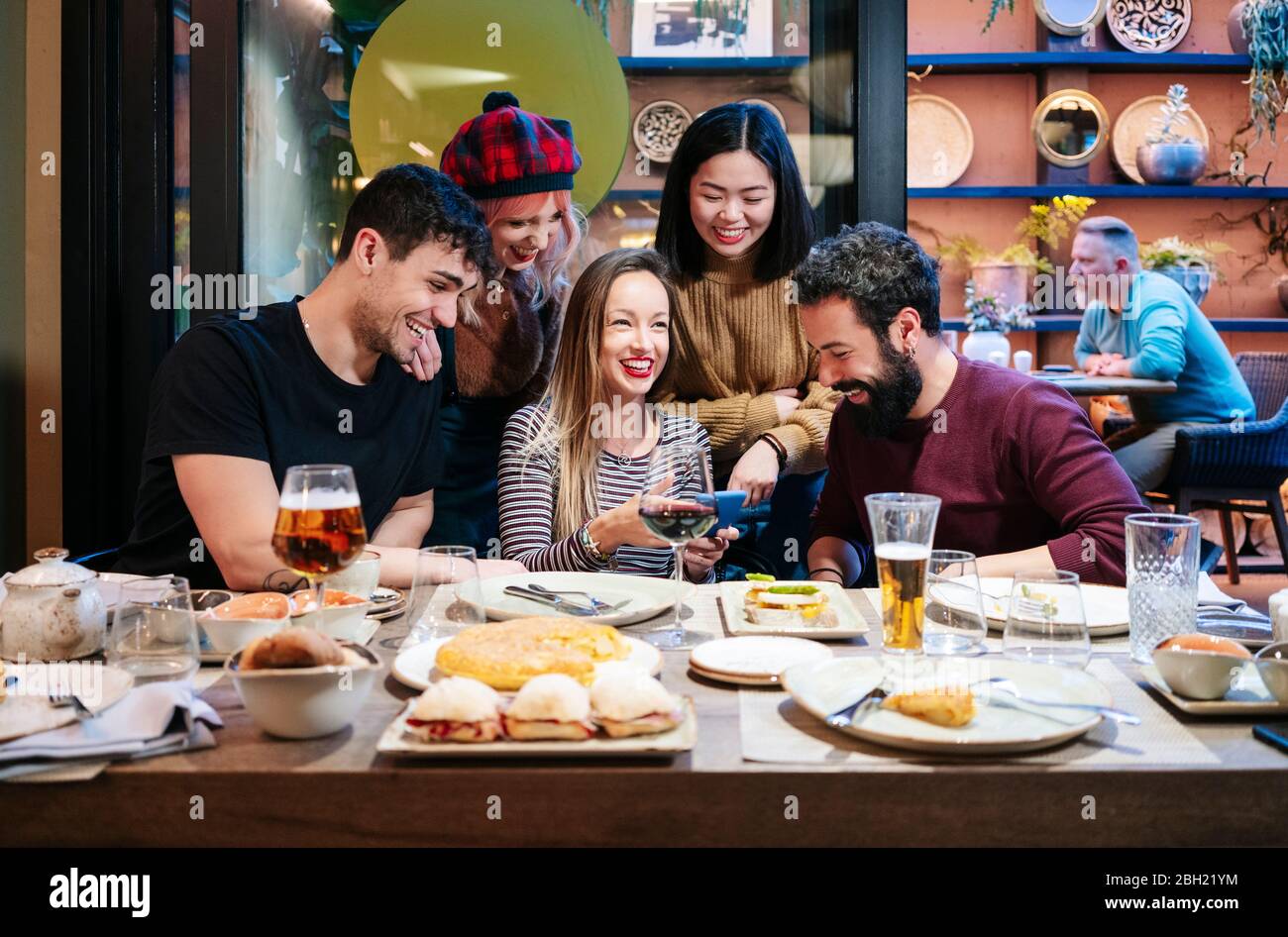 Friends having dinner in a fancy restaurant, looking at smartphone ...