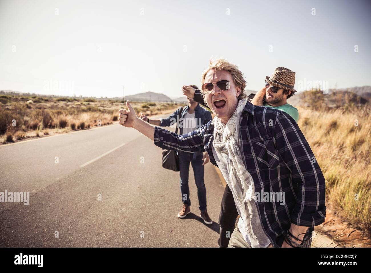 Three men hitchhiking at a country road Stock Photo - Alamy
