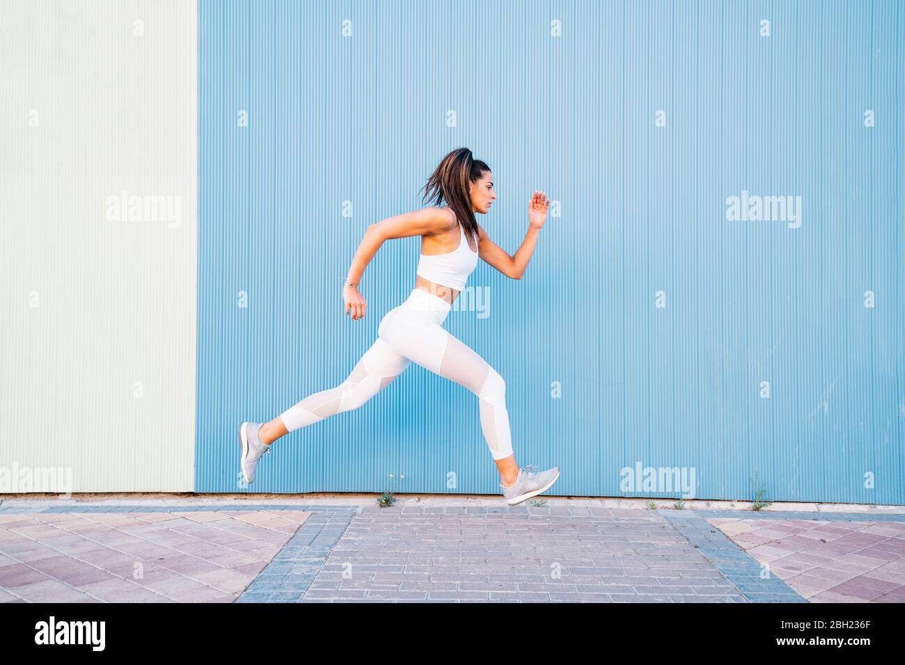 Young woman jogging in front of blue and green wall Stock Photo - Alamy