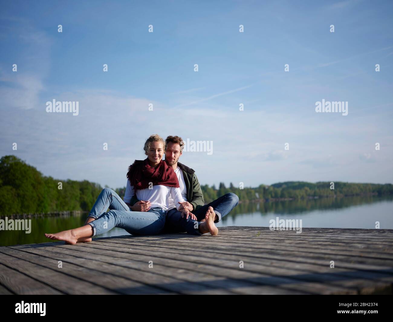 Romantic couple sitting on jetty at the lake Stock Photo - Alamy