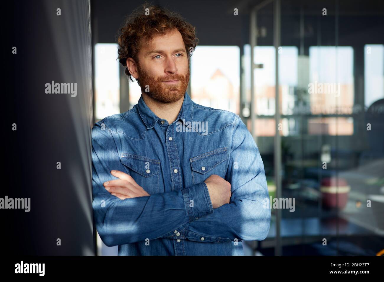 Portrait of a casual businessman leaning against a wall in office Stock ...