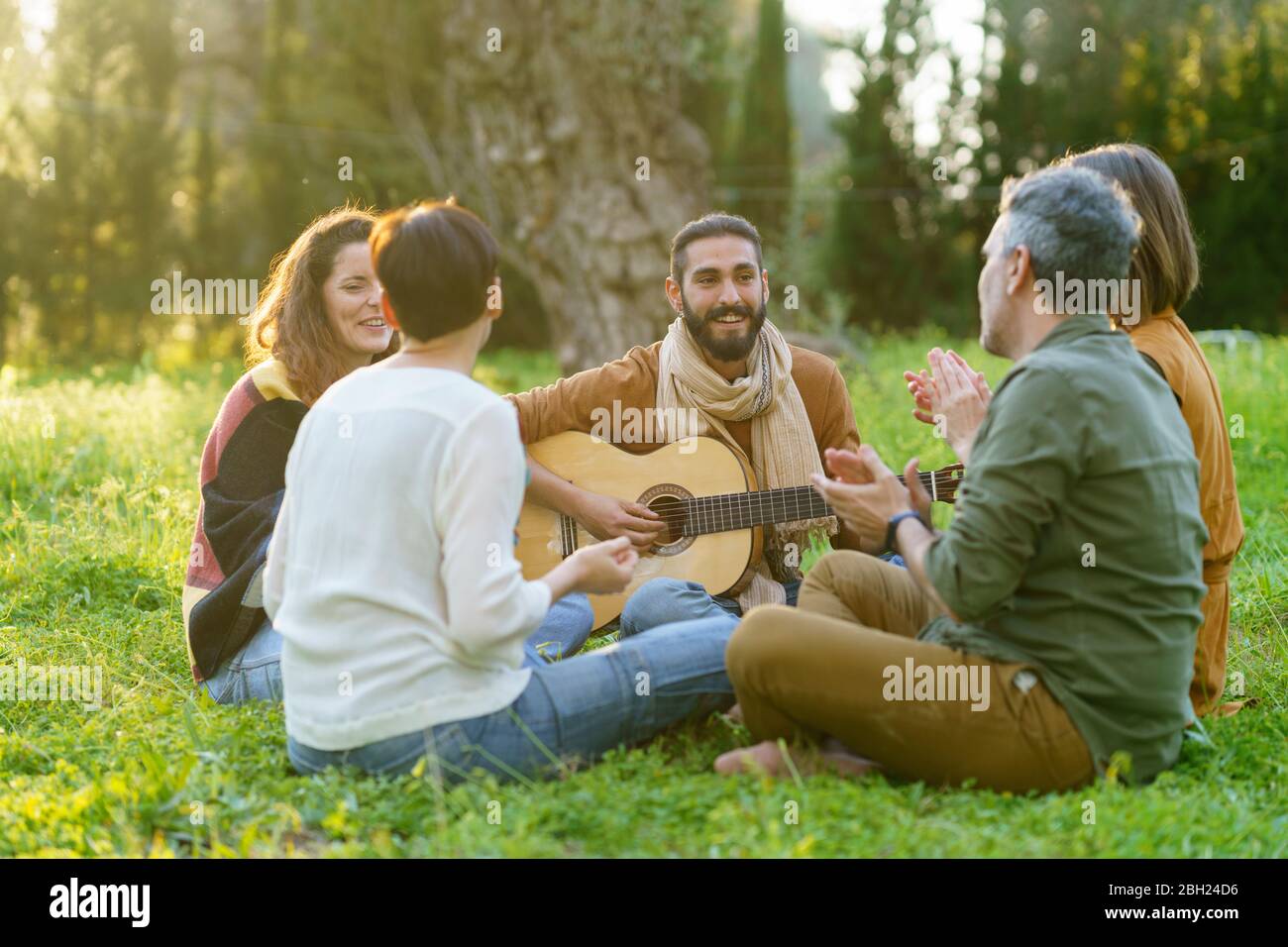Group of friends playing music with the guitar sitting on the grass in ...