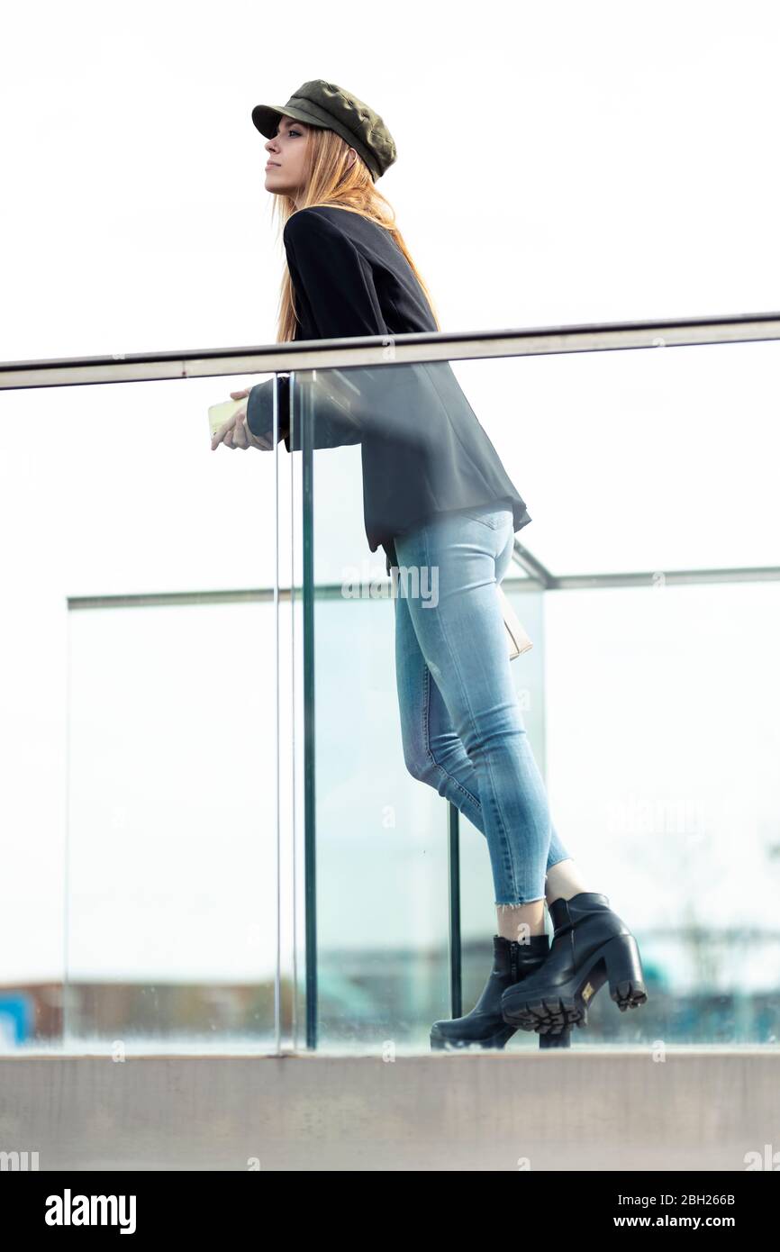 Portrait of blond young woman leaning on railing looking at distance ...